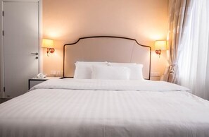 Quarto de hotel com uma cama grande, duas luminárias de cabeceira, uma mesa de cabeceira com telefone e uma porta.