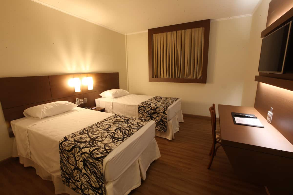 Quarto de hotel com duas camas, uma escrivaninha e uma televisão.