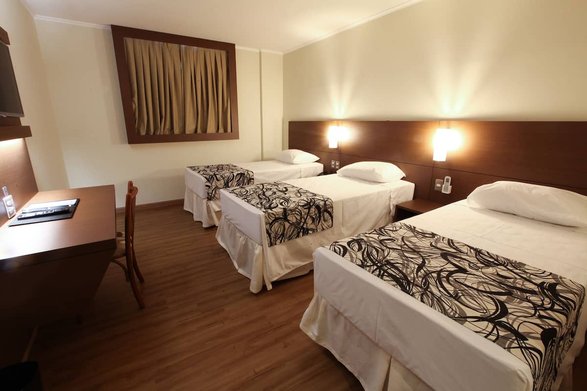Quarto de hotel com duas camas de solteiro, uma escrivaninha com cadeira e uma televisão.