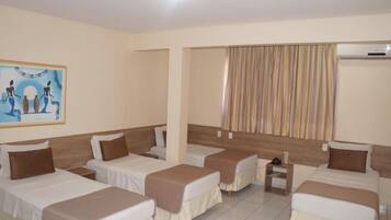 Quarto de hotel com quatro camas de solteiro, um quadro na parede, uma janela com cortinas e um aparelho de ar condicionado.