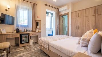 Quarto de hotel com cama, escrivaninha com computador, mini-geladeira, televisão e guarda-roupa.