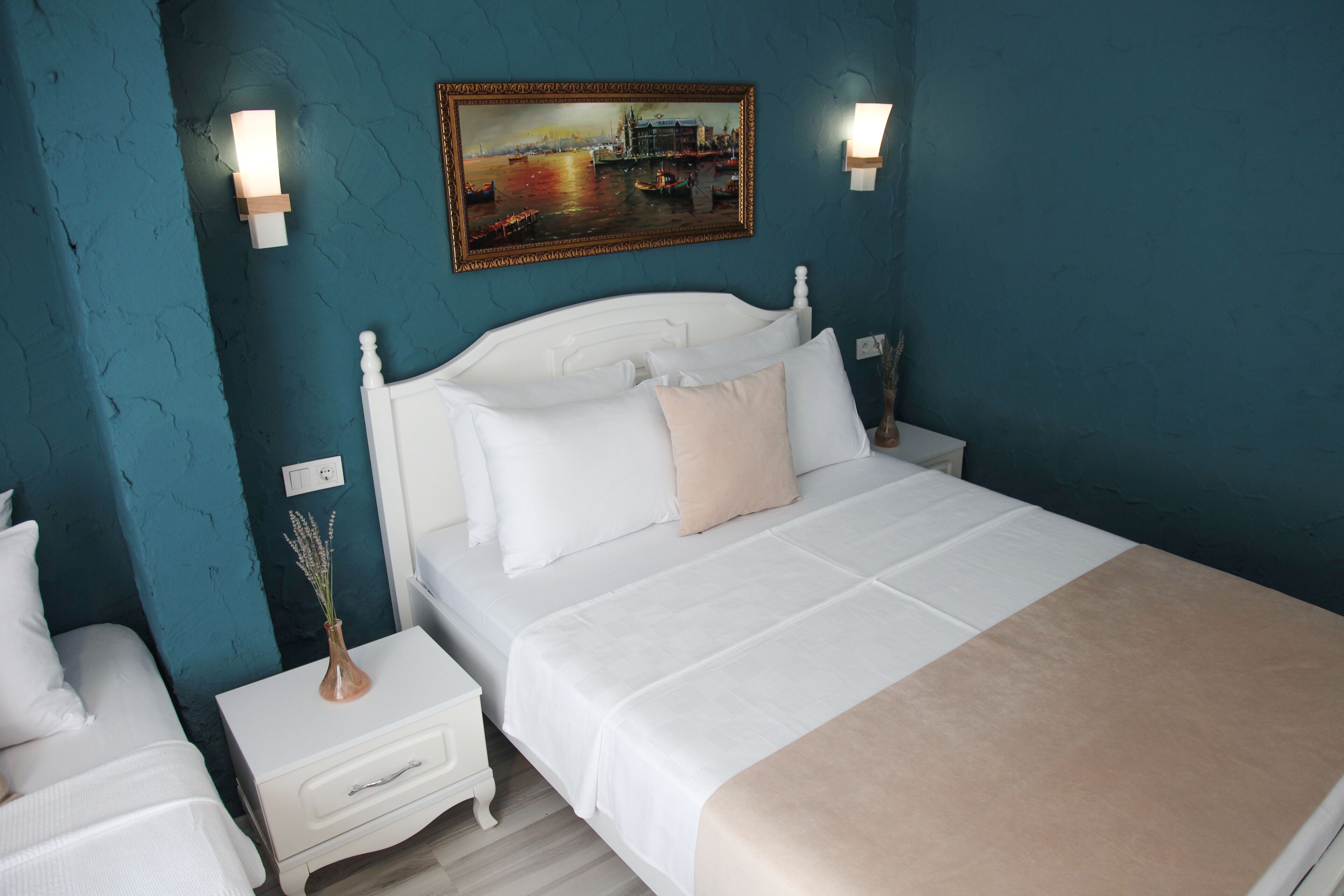 Quarto com cama grande, duas mesas de cabeceira, mesa de apoio e um vaso com flores, além de um quadro na parede.