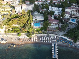 Vista aérea de um resort à beira-mar, com vários edifícios, piscina e área de praia com guarda-sóis e espreguiçadeiras.