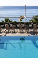 Área de piscina com espreguiçadeiras e vista para o mar.