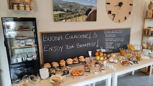 Um buffet de café da manhã com diversas opções de comida, um cardápio em lousa e um relógio na parede.