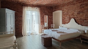 Quarto com parede de tijolos, piso de madeira, cama, guarda-roupa e janela com cortinas leves.