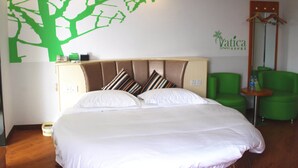 Quarto de hotel com cama, cabeceira, uma cadeira verde, uma mesa pequena e uma parede com adesivo de árvore.