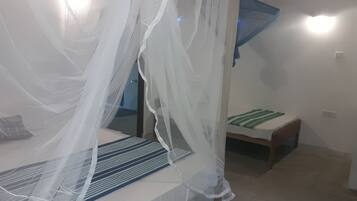 Quarto com cama sob um dossel branco, mesa de cabeceira com travesseiro listrado verde e branco, e um pequeno banco de madeira com travesseiro verde e branco.