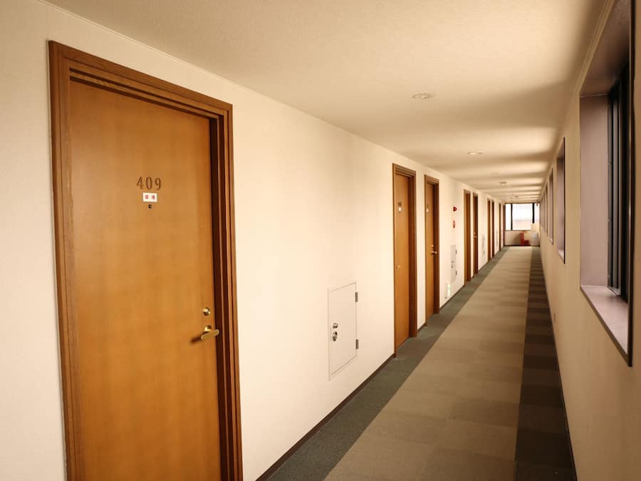 Corredor de hotel com portas de madeira, placas de números de quarto e piso coberto por carpete.