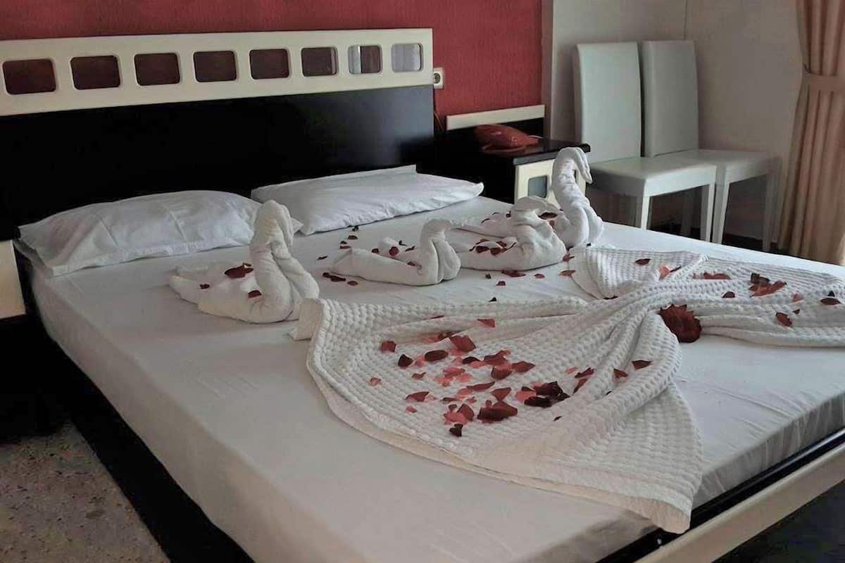 Quarto de hotel com cama, almofadas brancas, cabeceira preta e mesa de cabeceira branca com abajur.