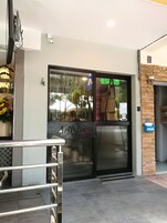 Entrada de hotel com porta de vidro, placa com a inscrição 'Artisan Eco Hotel' e sinal de saída azul.