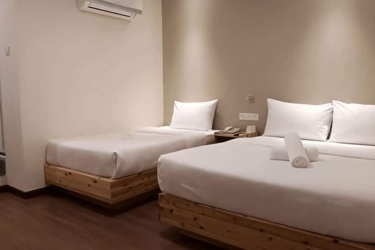 Quarto de hotel com duas camas, piso de madeira, ar-condicionado fixado na parede e mesa de cabeceira com telefone.