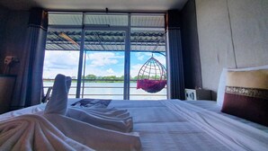 Quarto de hotel com cama, cadeira suspensa e vista para a água.