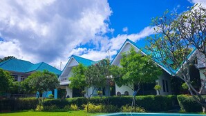 Vista da piscina de um resort, com vários edifícios, céu azul límpido e vegetação exuberante.