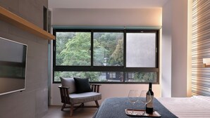 Quarto moderno com janela ampla, televisão de tela plana, cadeira de madeira, cama e garrafa de vinho sobremesa.