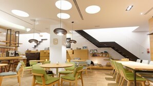 Uma sala de jantar moderna com mesas redondas e cadeiras verdes, uma escada e uma área de cozinha com armários de madeira.