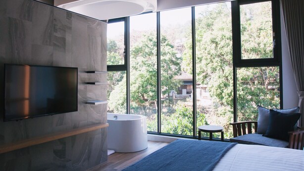 Quarto moderno com uma grande janela, televisão de tela plana, banheira e um espaço de estar acolhedor.