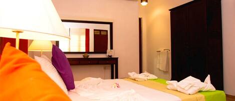 Quarto de hotel com cama, escrivaninha com abajur, espelho, ar condicionado e guarda-roupa.