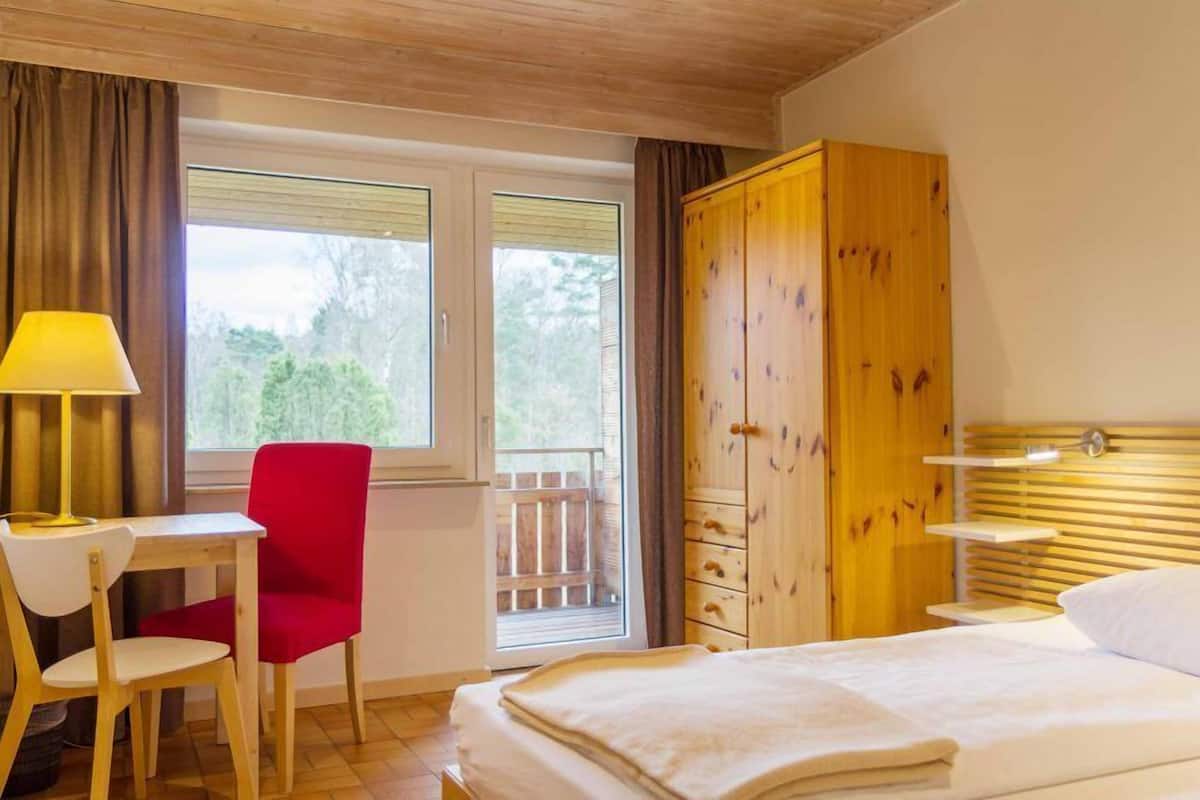 Quarto de hotel com cama, guarda-roupa de madeira, escrivaninha com cadeira e janela com cortinas.
