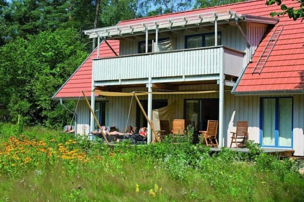 Uma casa de dois andares com telhado vermelho, varanda e varanda coberta com cadeiras.