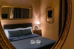 Cama bem arrumada com almofadas, mesa de cabeceira com abajur e bandeja com xícaras e bule.
