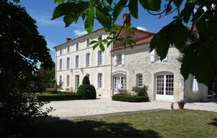Um edifício de pedra de dois andares com arquitetura europeia clássica, apresentando um pátio central, um jardim bem cuidado e uma entrada visível com porta e janelas.