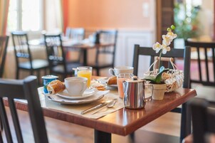 Uma mesa de café da manhã com um croissant, xícara de café, suco e uma pequena planta em vaso.