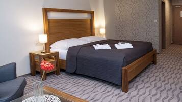 Quarto de hotel com cama de madeira, duas luminárias de cabeceira, uma mesinha com um vaso e um tapete estampado.