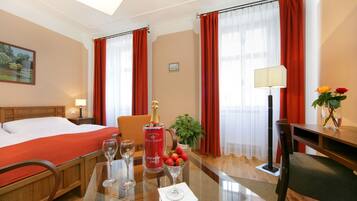 Quarto de hotel com uma cama, uma mesa com champanhe, copos, morangos e uma planta em vaso.