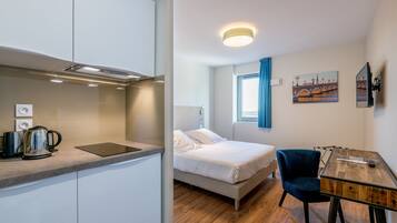 Quarto de hotel compacto com cozinha compacta, uma cama, uma escrivaninha e uma cadeira.