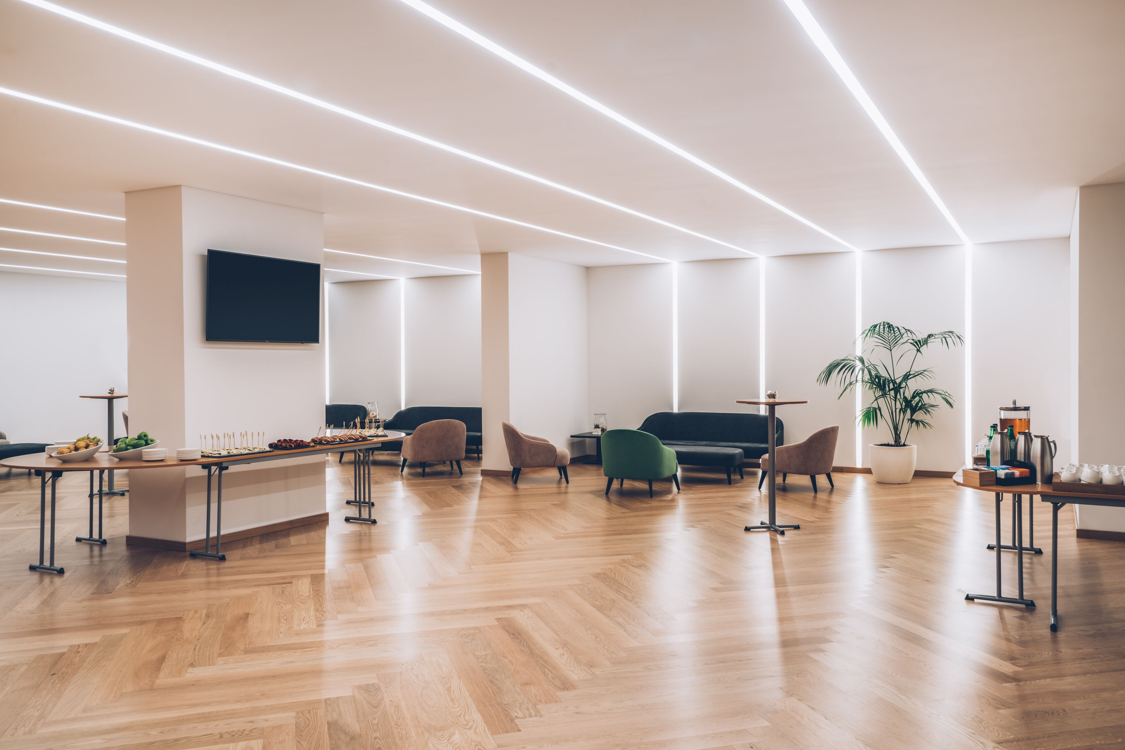 Uma área de estar espaçosa e moderna, com uma mesa de madeira comprida, várias cadeiras, um sofá e um vaso com planta.