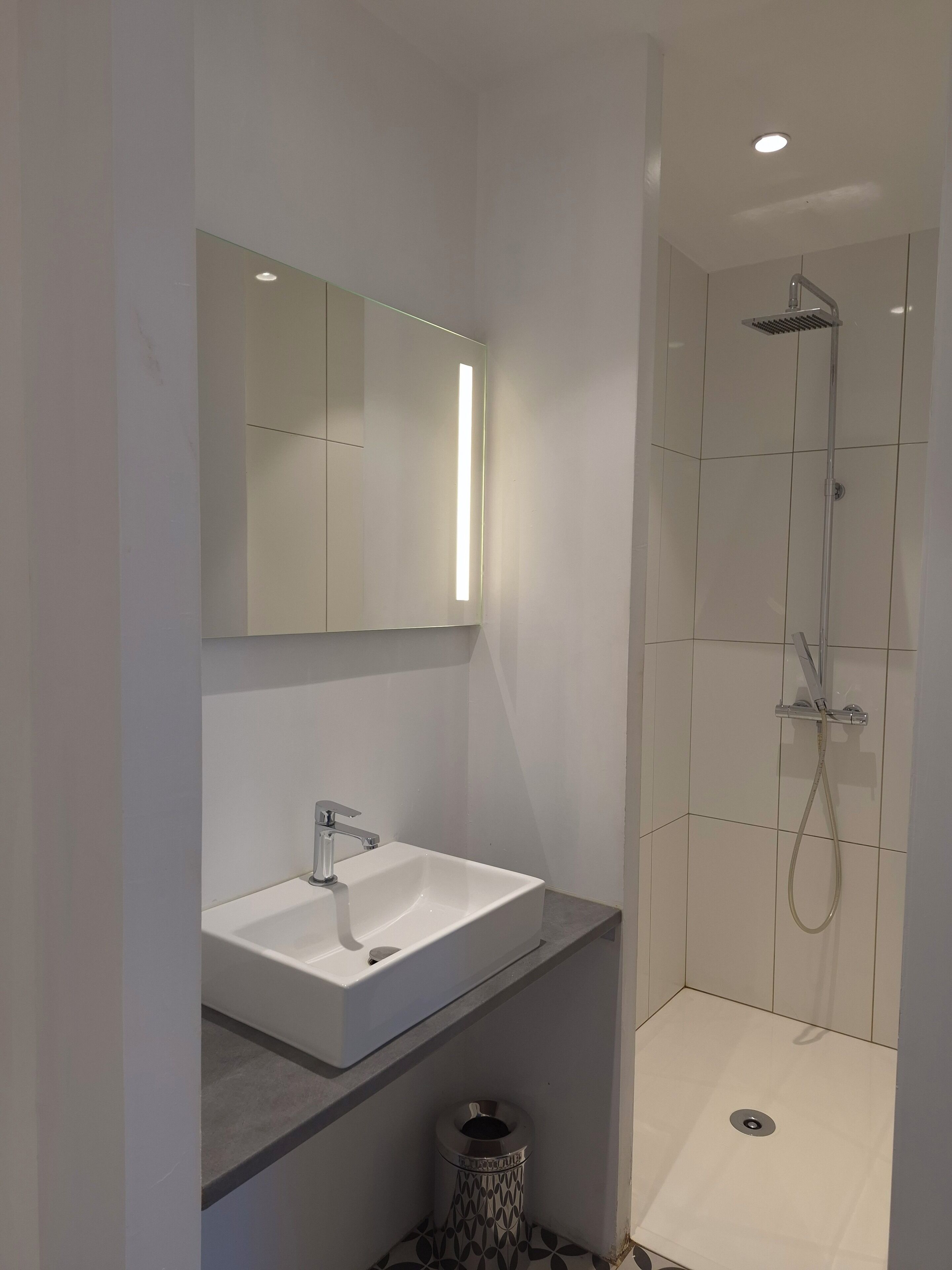 Uma casa de banho moderna com uma pia branca, um espelho e um chuveiro.