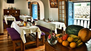Uma sala de jantar com mesas preparadas para o café da manhã, uma apresentação de frutas e vista para o exterior.