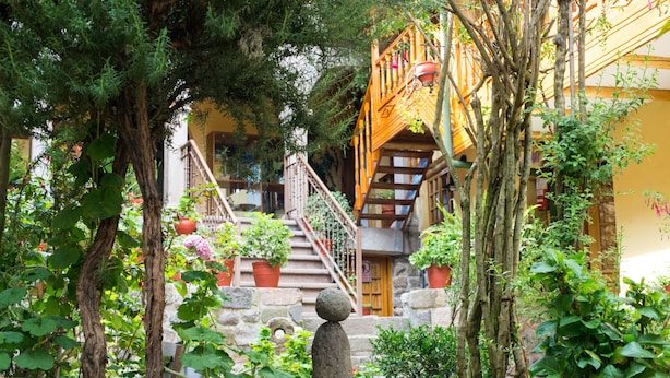 Escadaria de pedra que leva a uma porta de madeira, cercada por vegetação exuberante e plantas em vasos.