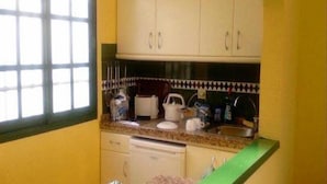 Uma cozinha compacta com armários brancos, bancada de granito e uma janela com persianas.