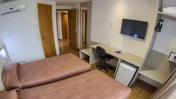 Quarto de hotel com duas camas, uma escrivaninha com cadeira, televisão e um pequeno frigorífico.