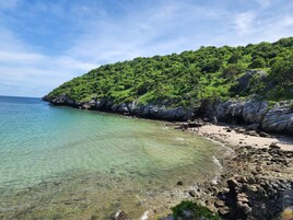 Uma praia costeira com águas cristalinas, costa rochosa e colinas verdejantes.