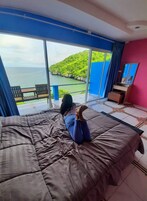 Quarto com cama grande, vista para o mar e varanda com mesa e cadeiras.