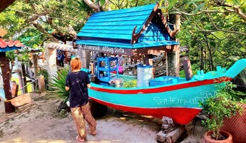 Uma estrutura em forma de barco com teto azul e detalhes vermelhos, cercada por vegetação.