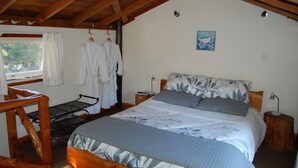 Quarto com teto de madeira, cama com roupa de cama floral, mesa de cabeceira com abajur e janela com cortinas.