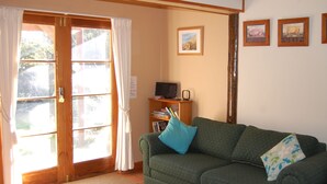 Uma sala de estar acolhedora com um sofá verde, uma estante de madeira e uma porta que dá para um jardim.