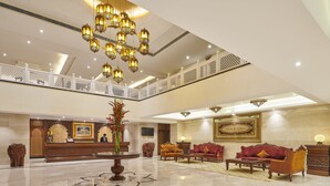Um hall amplo com teto alto, lustres elaborados, balcão de recepção e áreas de estar confortáveis.