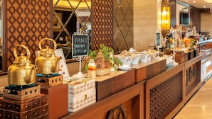 Um balcão de buffet com bules tradicionais, uma placa com a inscrição "PANI YARAM STATION" e uma variedade de comidas.