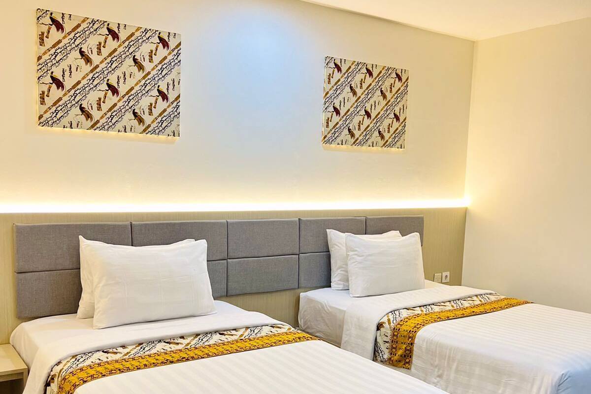 Quarto de hotel com duas camas, cabeceira cinza e painel de parede estampado.