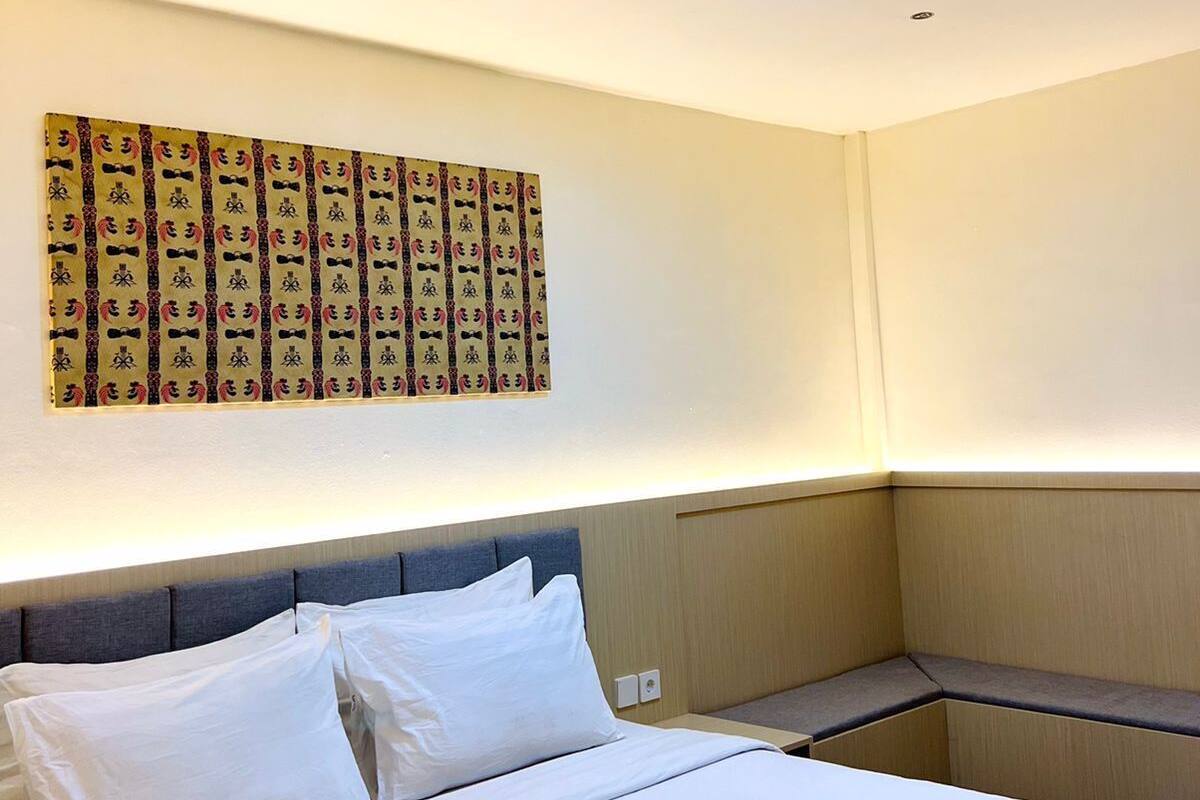 Quarto de hotel com cama bem arrumada, cabeceira e uma obra de arte na parede.