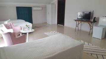 Quarto de hotel com cama, escrivaninha, cadeira, televisão e frigorífico.