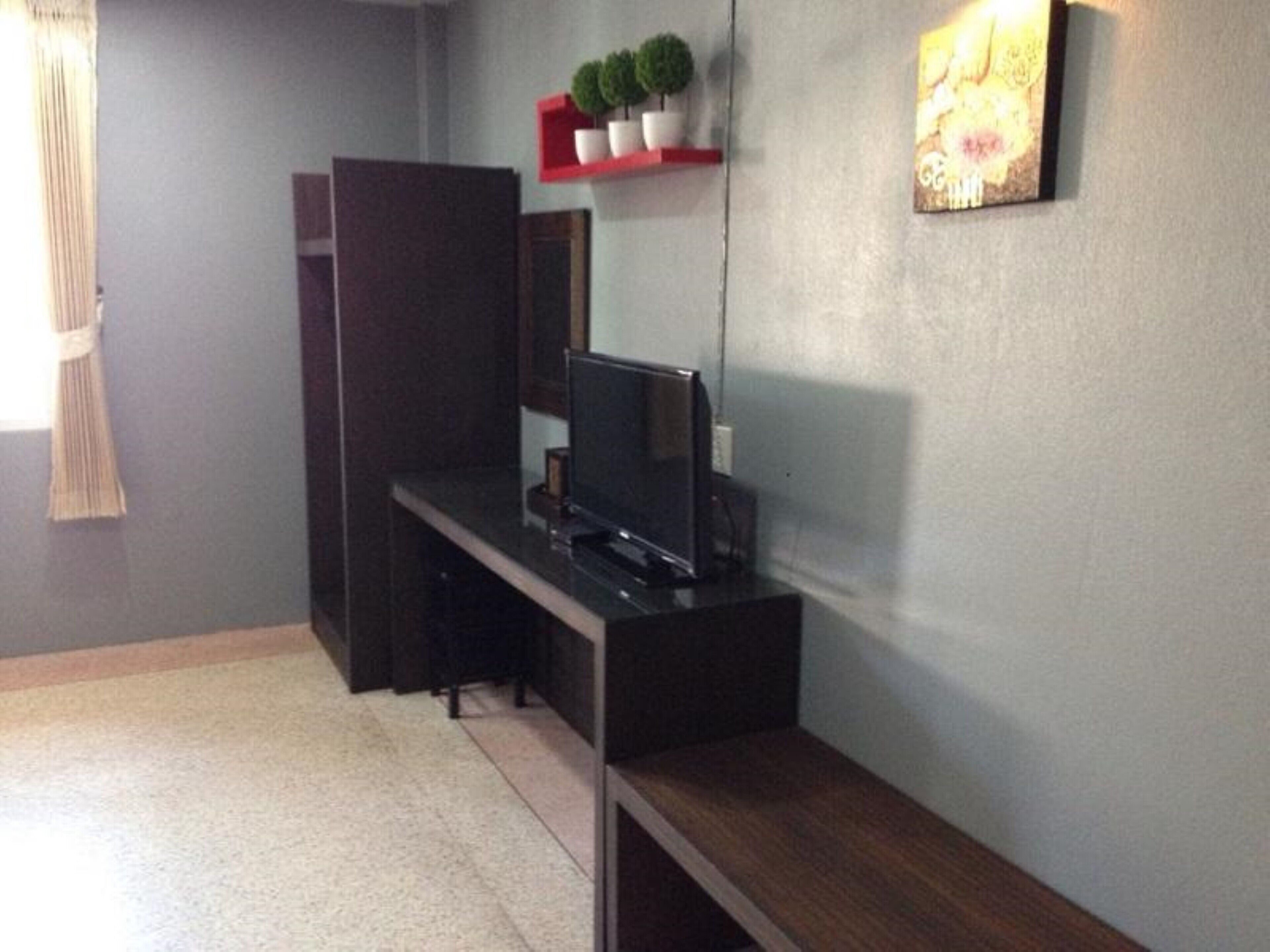 Quarto com um móvel de entretenimento escuro, uma televisão de tela plana e uma pequena estante com plantas em vasos.