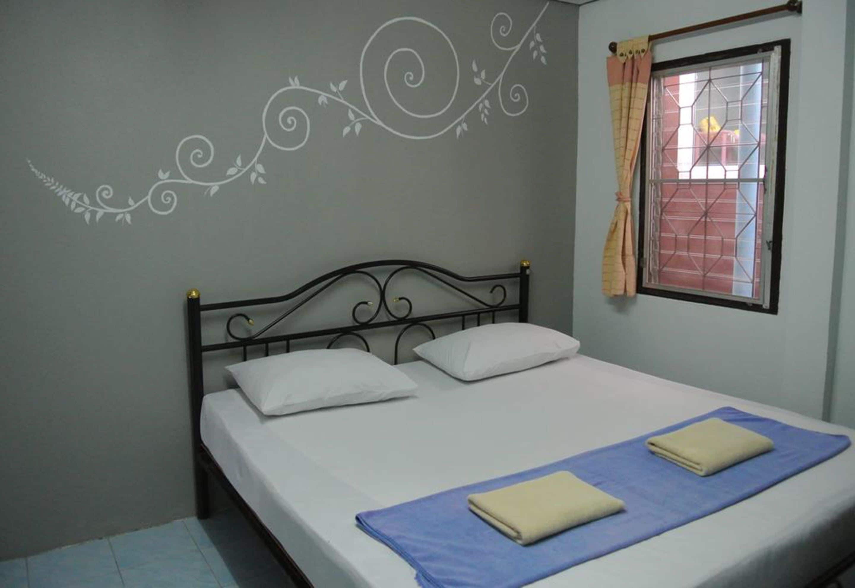Uma cama de solteiro com estrutura metálica, roupa de cama branca e duas toalhas dobradas sobre um tapete azul.