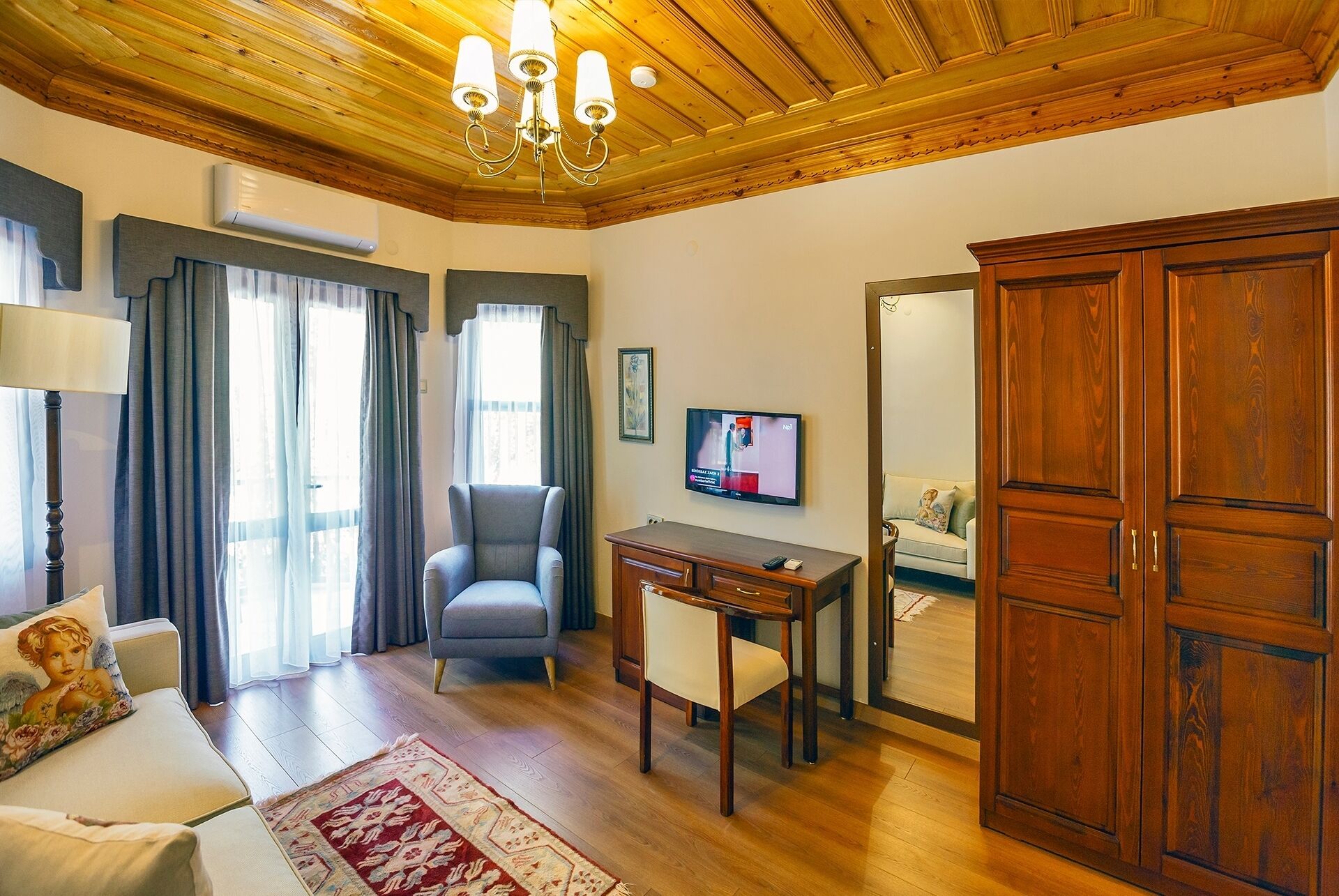 Quarto com teto de madeira, televisão, escrivaninha, cadeira, sofá e guarda-roupa.