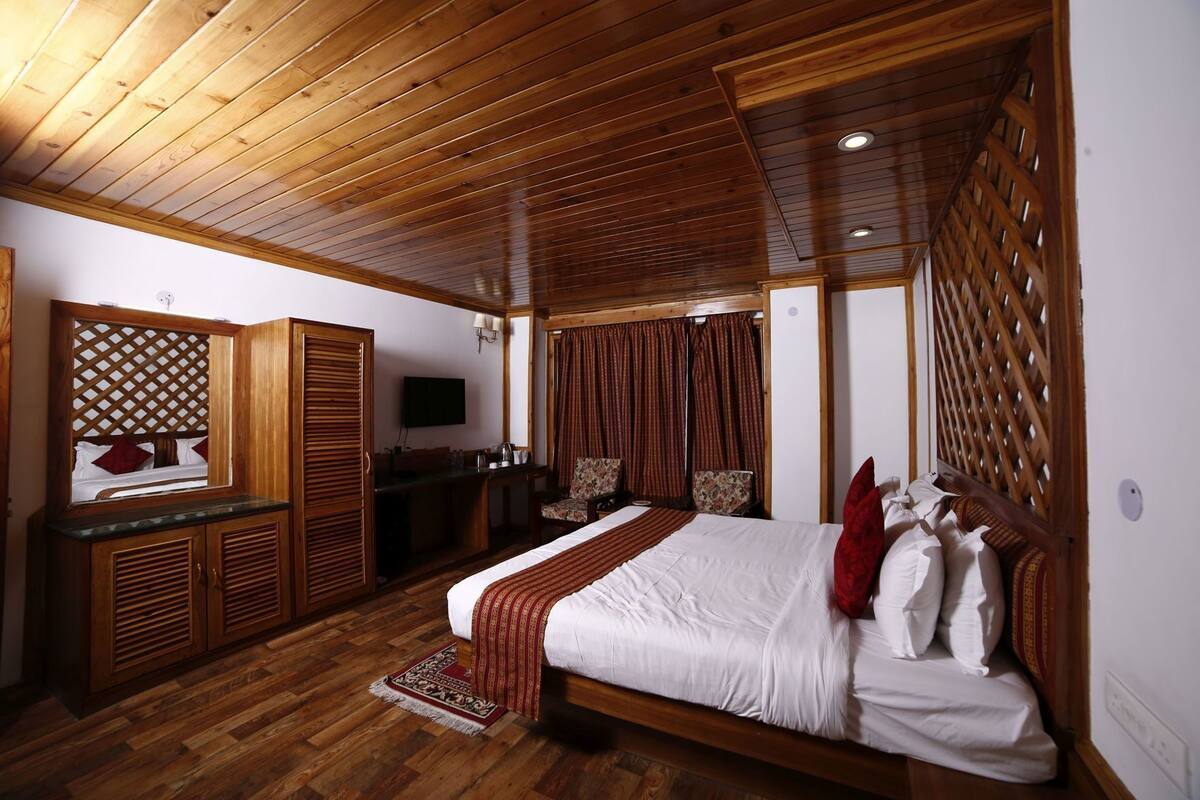 Quarto com painéis de madeira, uma cama, escrivaninha, televisão e guarda-roupa.